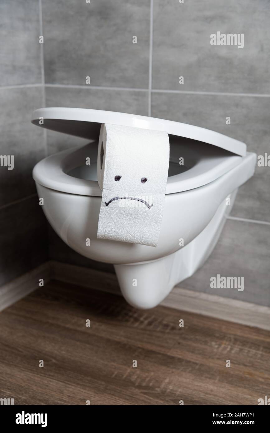 Sad emoticon on white toilet paper on toilet bowl in modern restroom ...