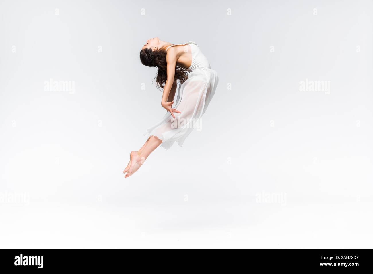 side view of graceful young ballerina jumping in dance on grey ...