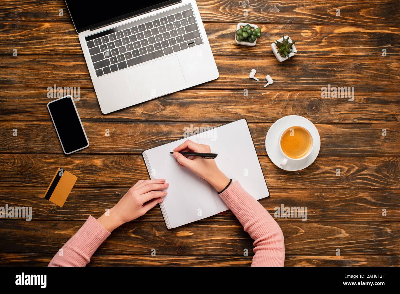 cropped view of businesswoman writing in notebook near laptop ...