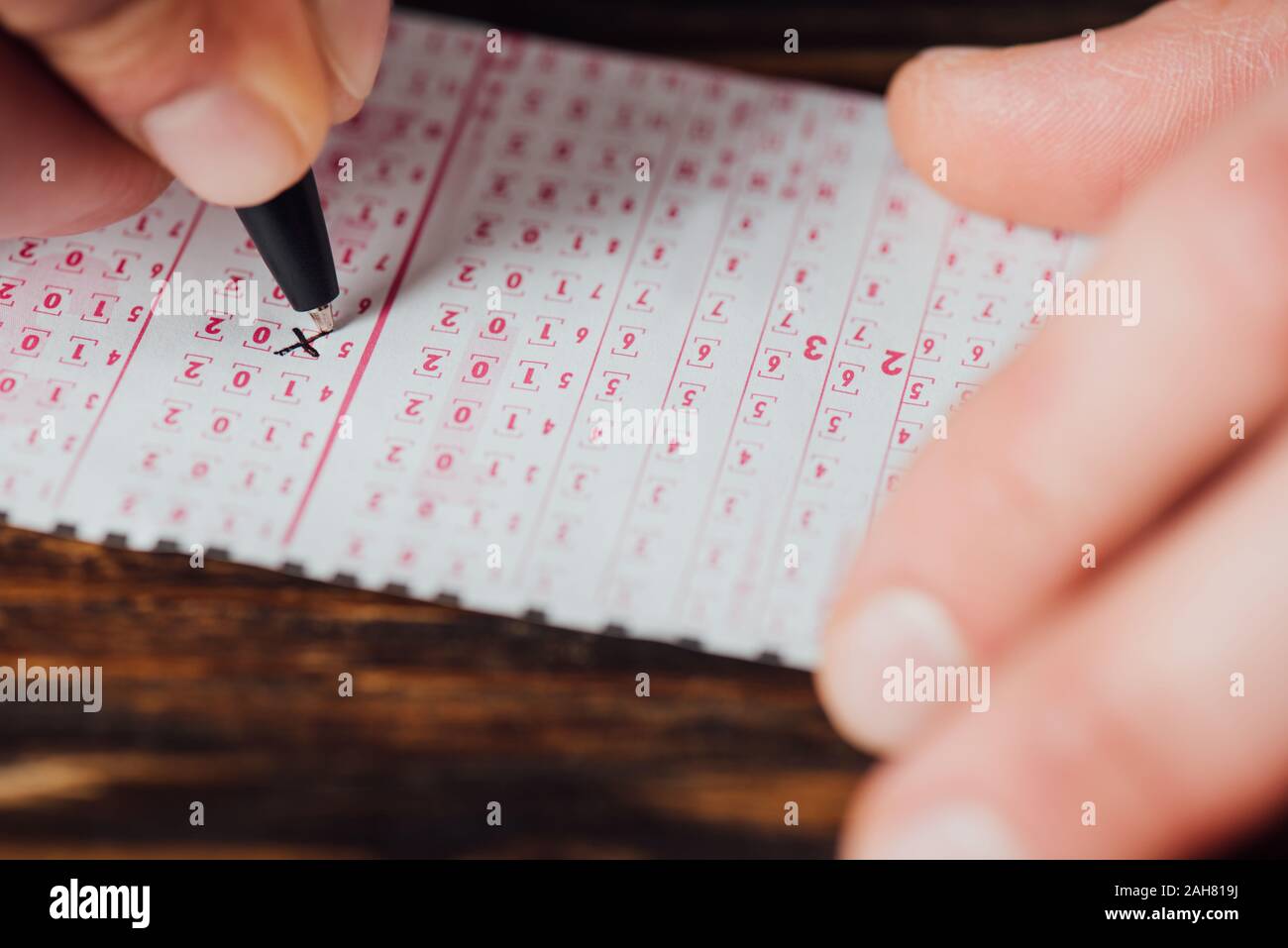 selective focus of gambler marking numbers in lottery ticket with pen ...