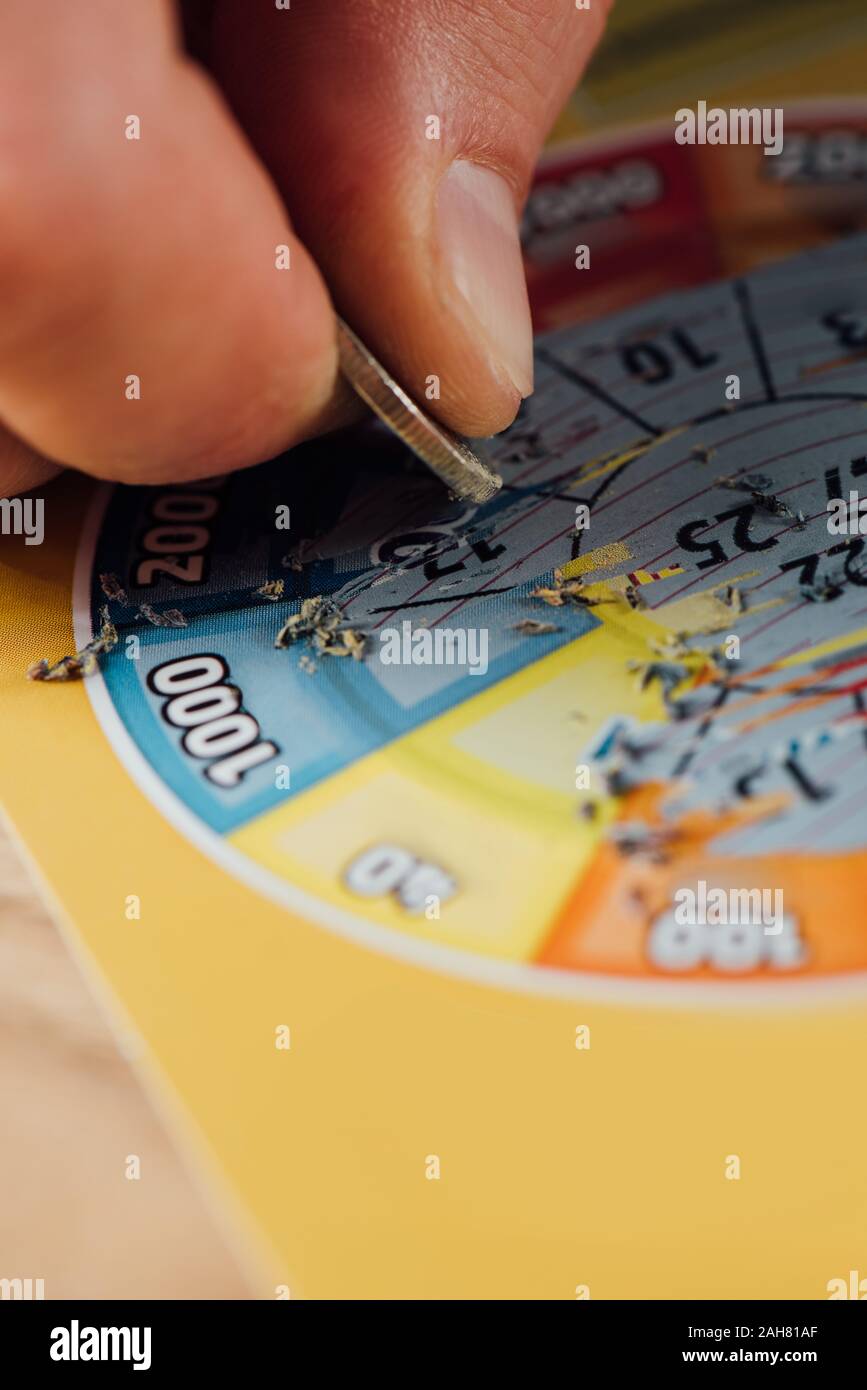 partial view of gambler scratching lottery ticket with silver coin ...