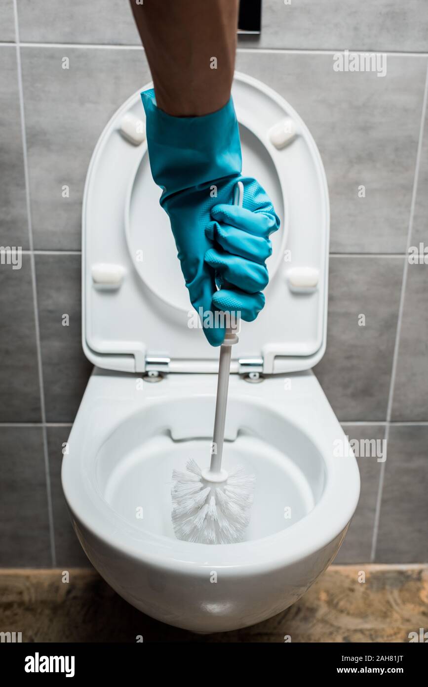 cropped view of cleaner cleaning ceramic toilet bowl with toilet brush ...