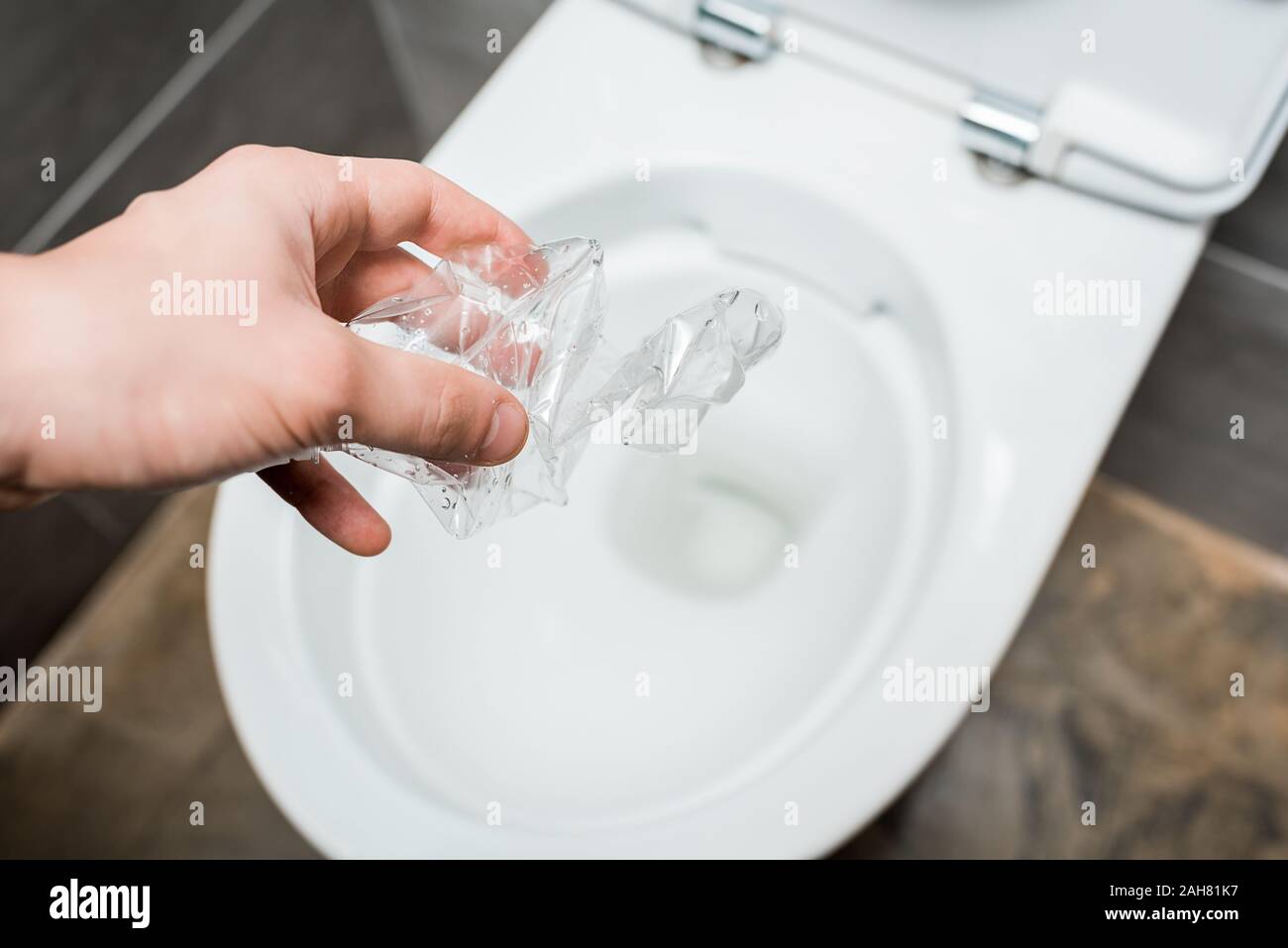 cropped view of man throwing crumpled plastic bottle in toilet bowl in ...
