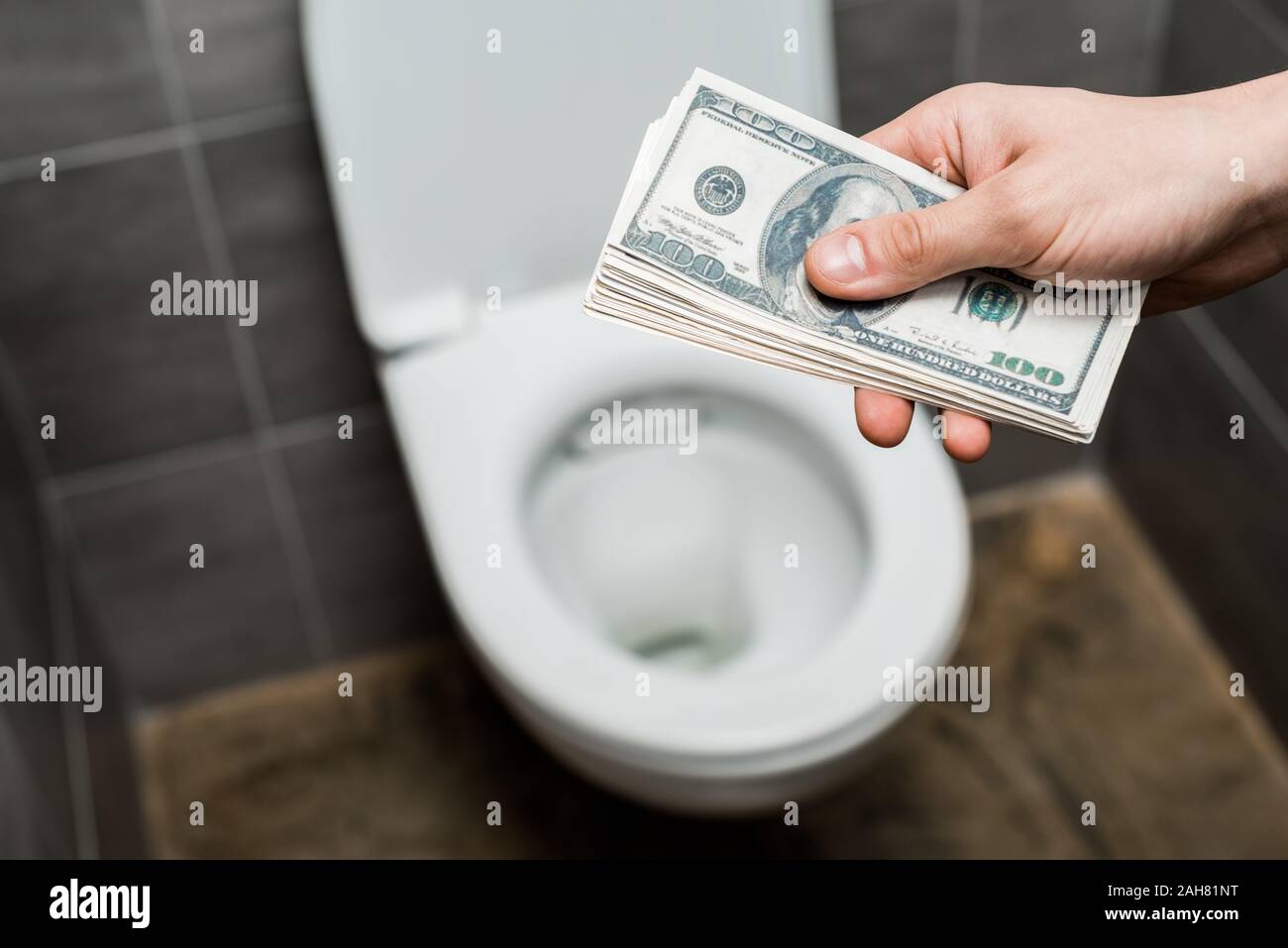 cropped view of man holding dollar banknotes near toilet bowl in modern ...