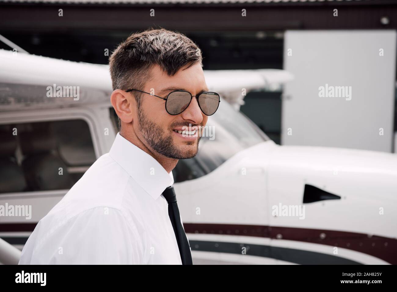 bearded pilot in formal wear and sunglasses smiling near plane Stock ...