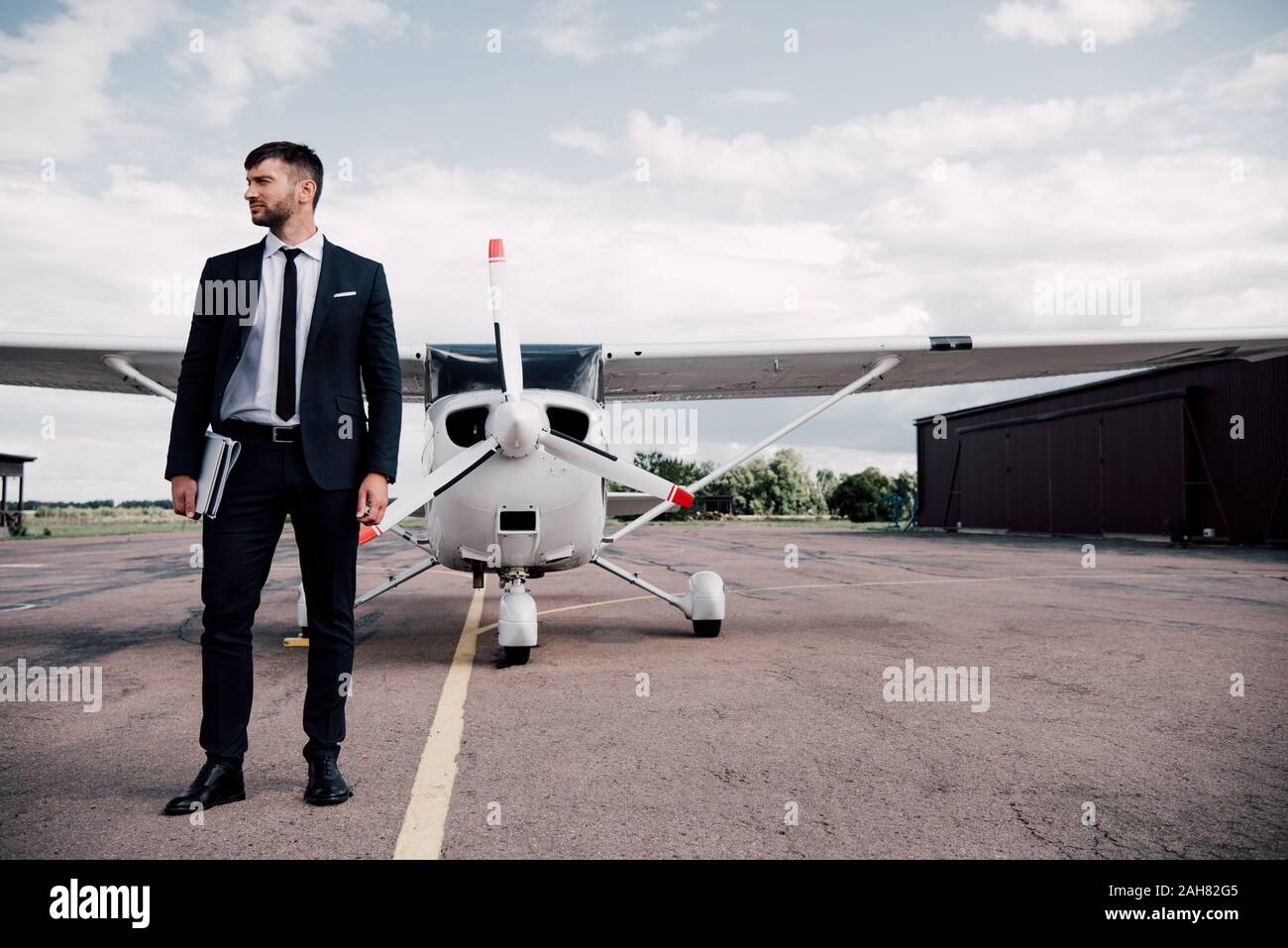 full length view of businessman in formal wear holding laptop near ...