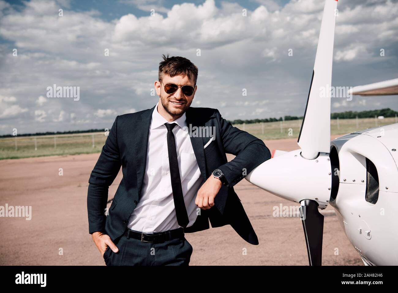 smiling businessman in formal wear standing with hand in pocket near ...