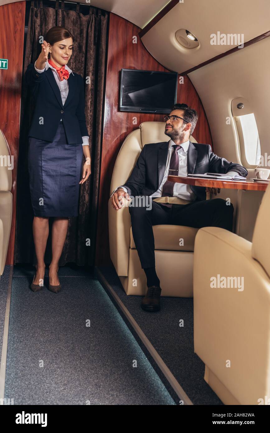 flight attendant showing gesture to handsome businessman in suit in ...