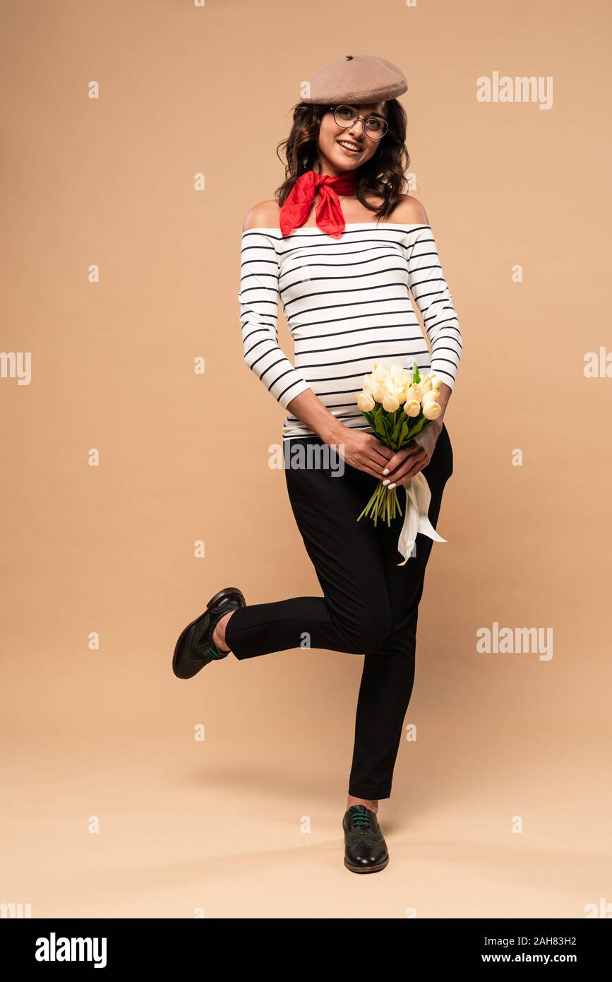 pregnant french woman in beret holding bouquet on beige background ...