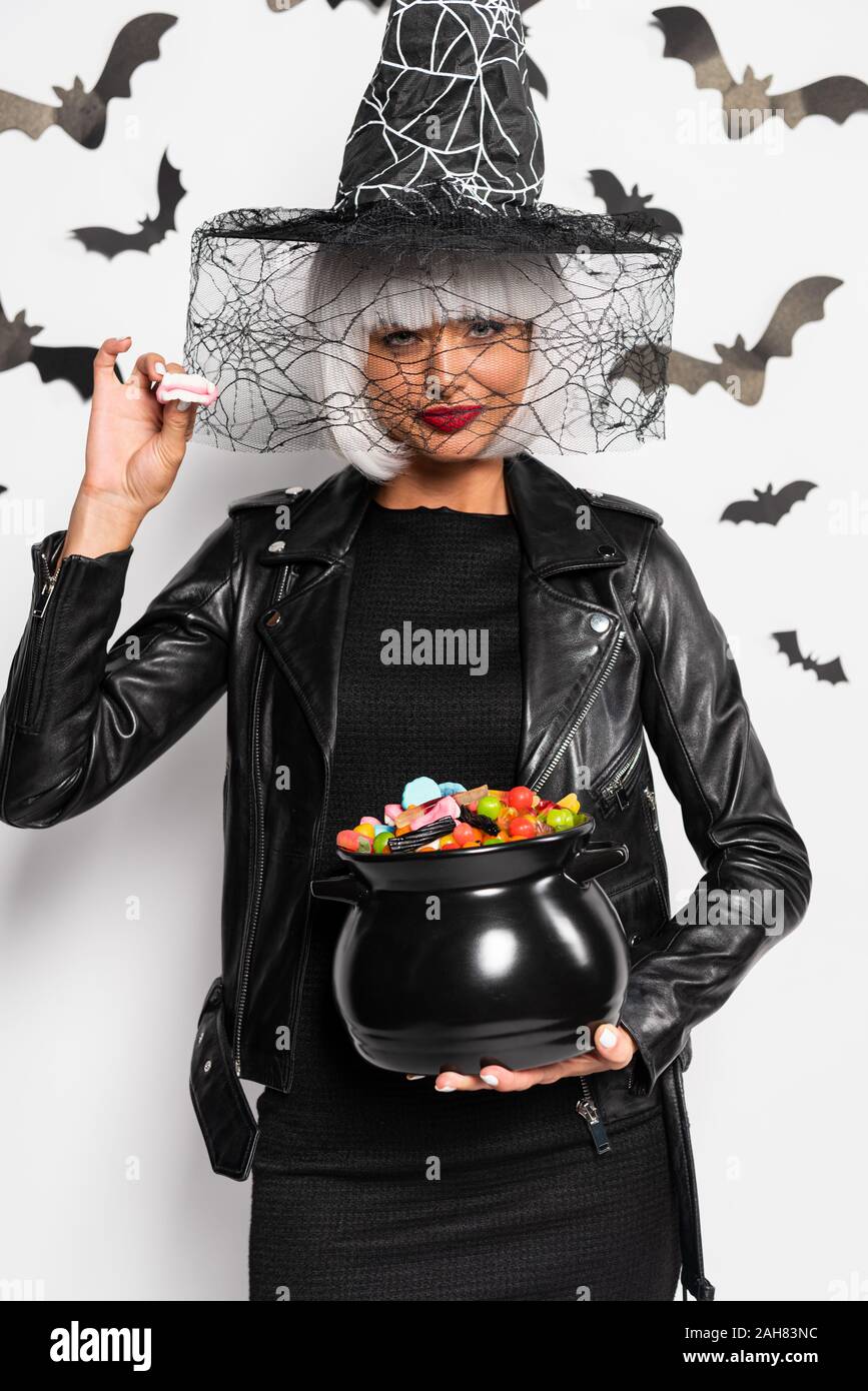attractive woman in witch hat and wig holding pot with candies in ...