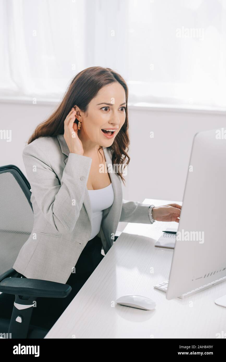 excited, surprised secretary looking at computer monitor while sitting ...