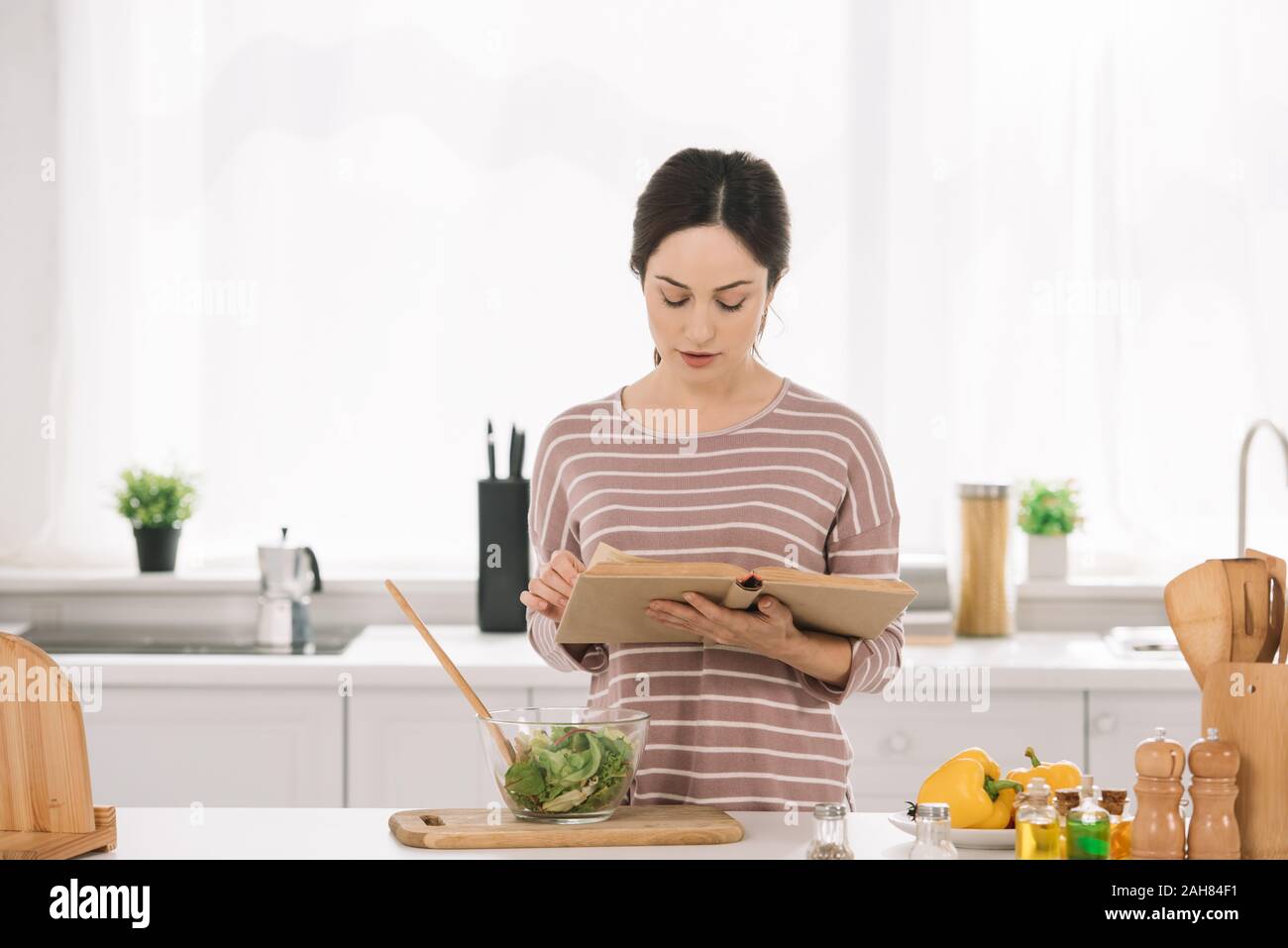 attractive, young woman reading receipt book while standing at kitchen ...