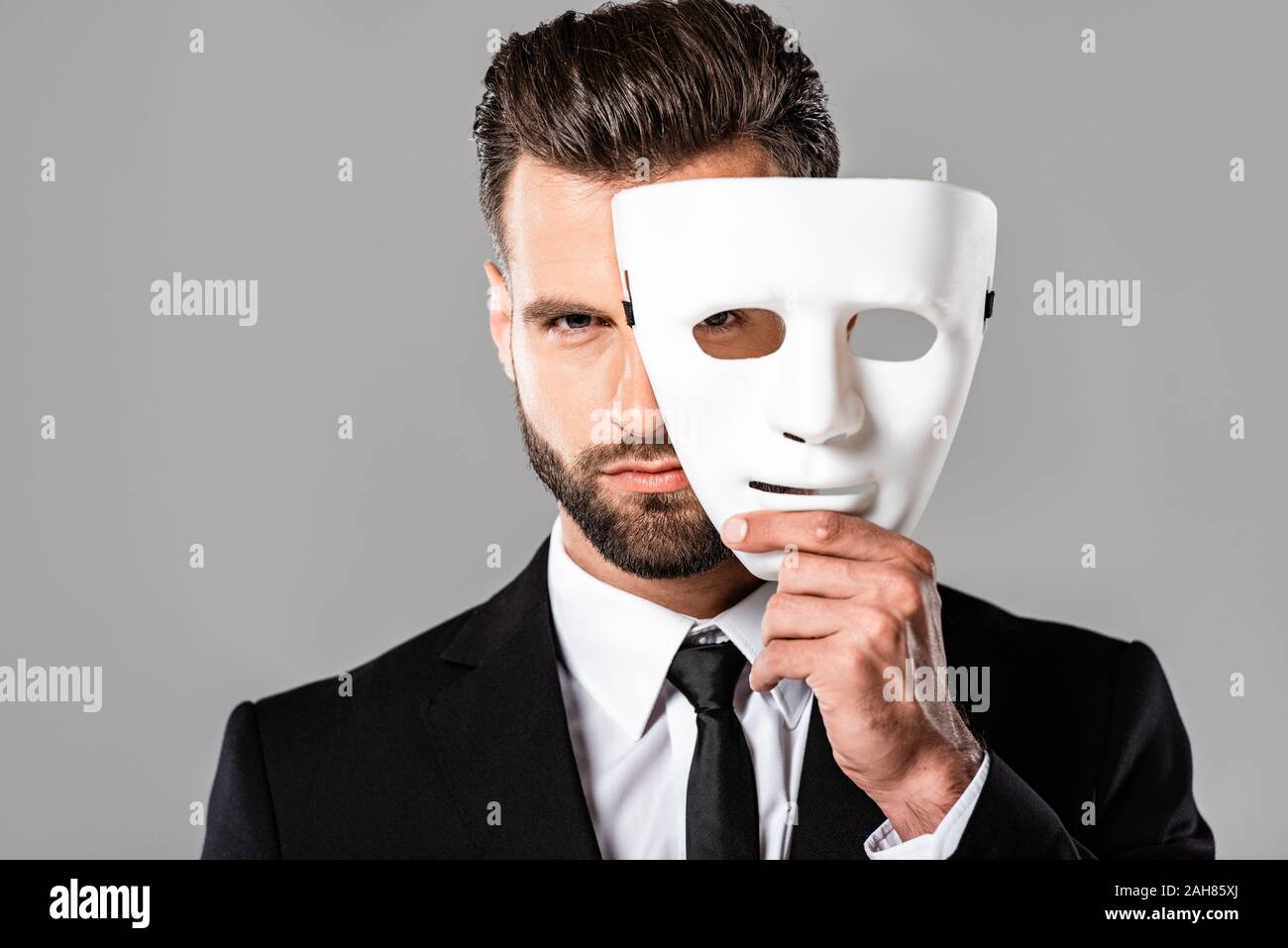 serious handsome businessman in black suit taking off white mask ...