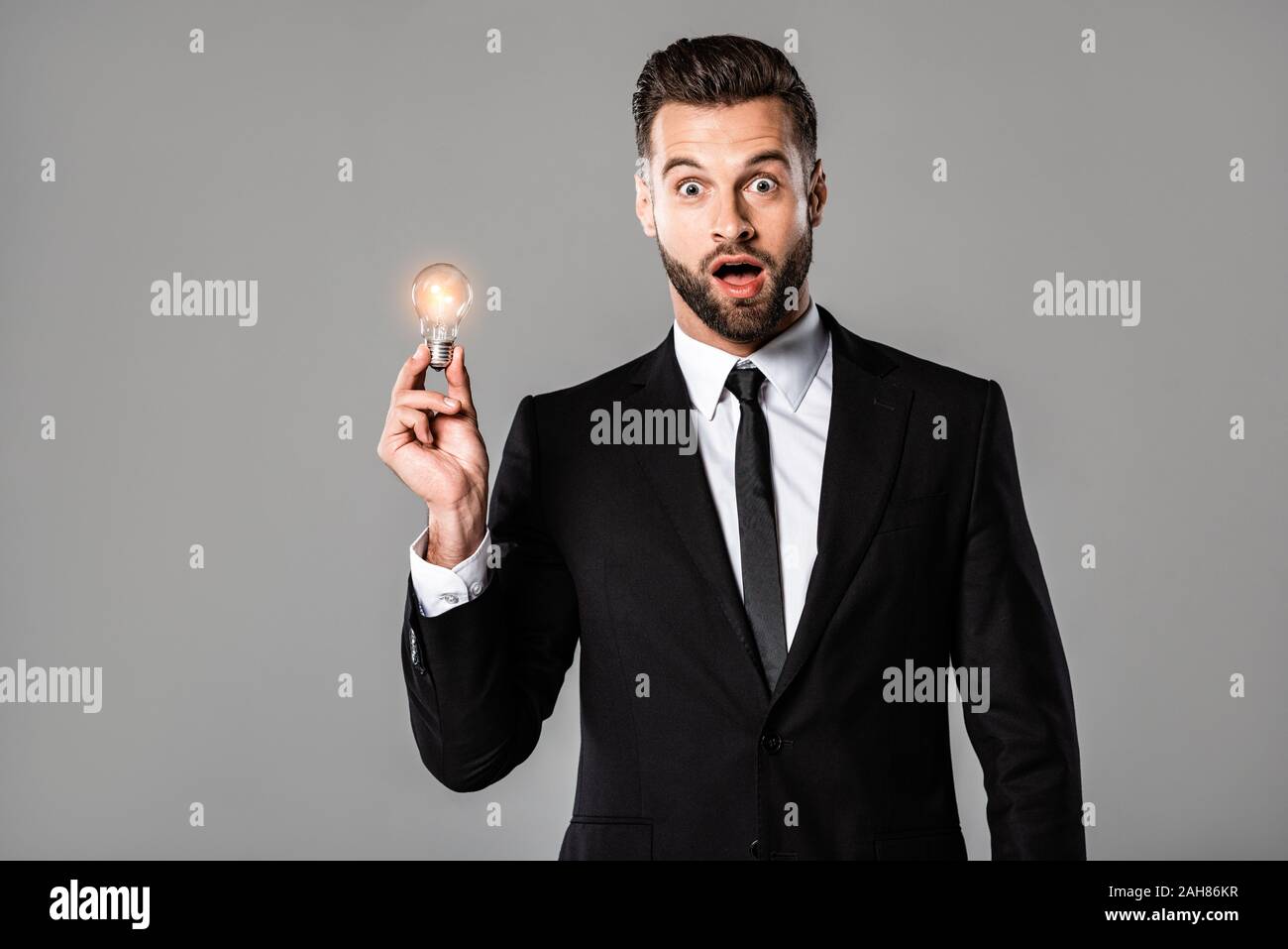 shocked businessman in black suit holding glowing light bulb isolated ...