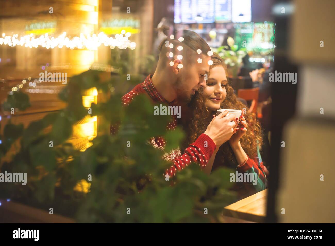 Loving couple in a cafe hug and drink cocoa. Photo from the street ...