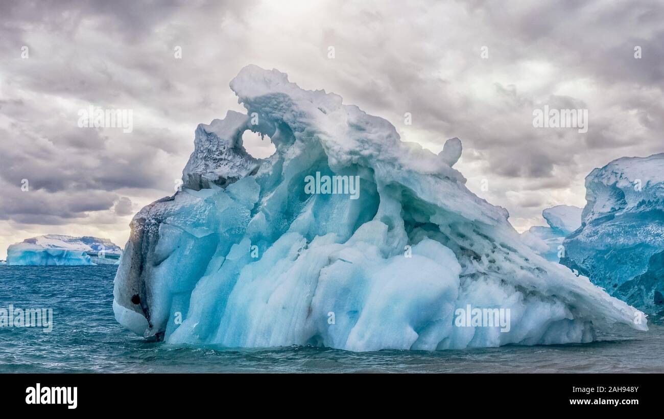 Close up of turquoise blue iceberg with small round hole at the top ...