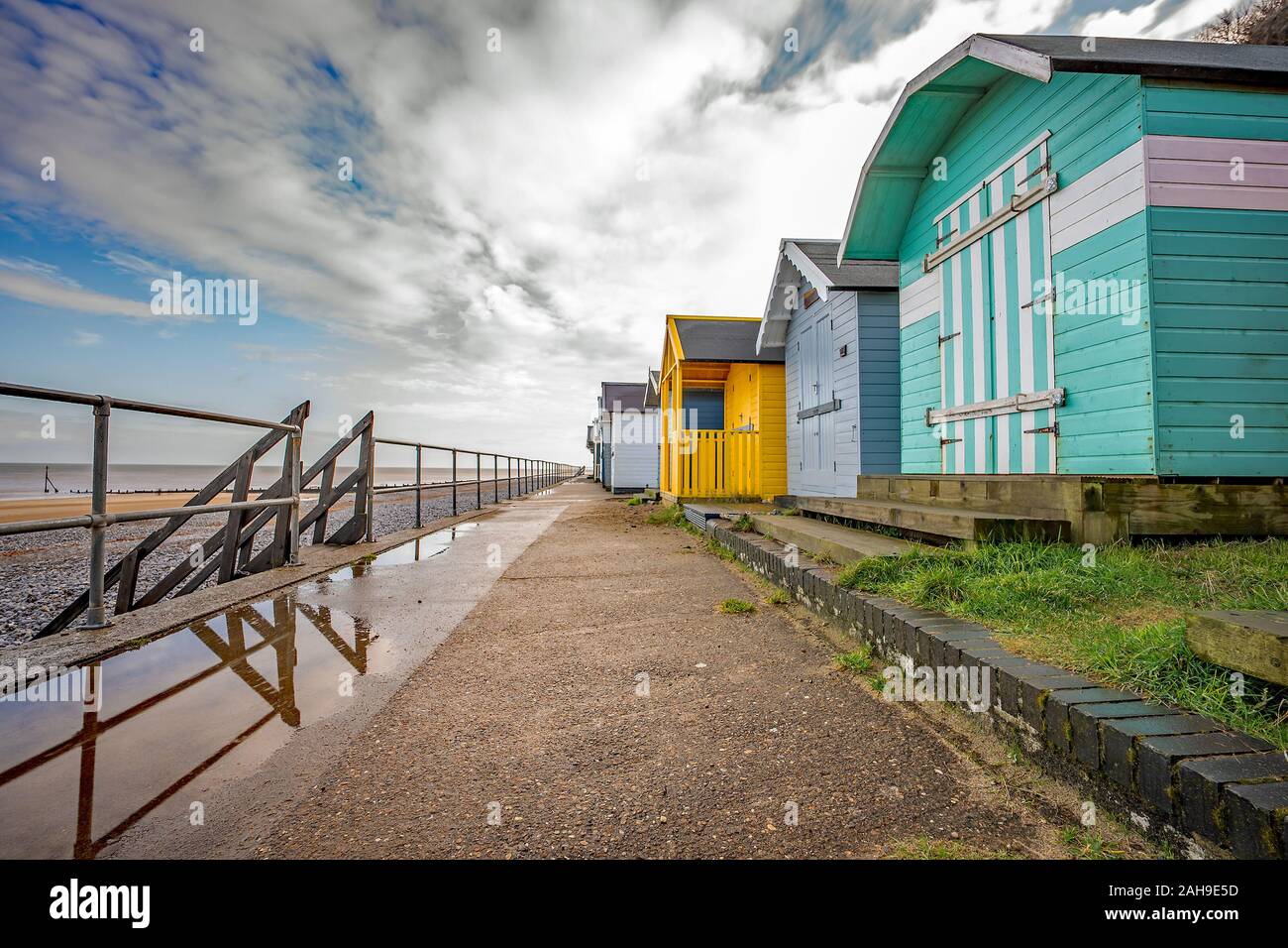 Row of traditional wooden beach huts on the promenade beside a sand and ...