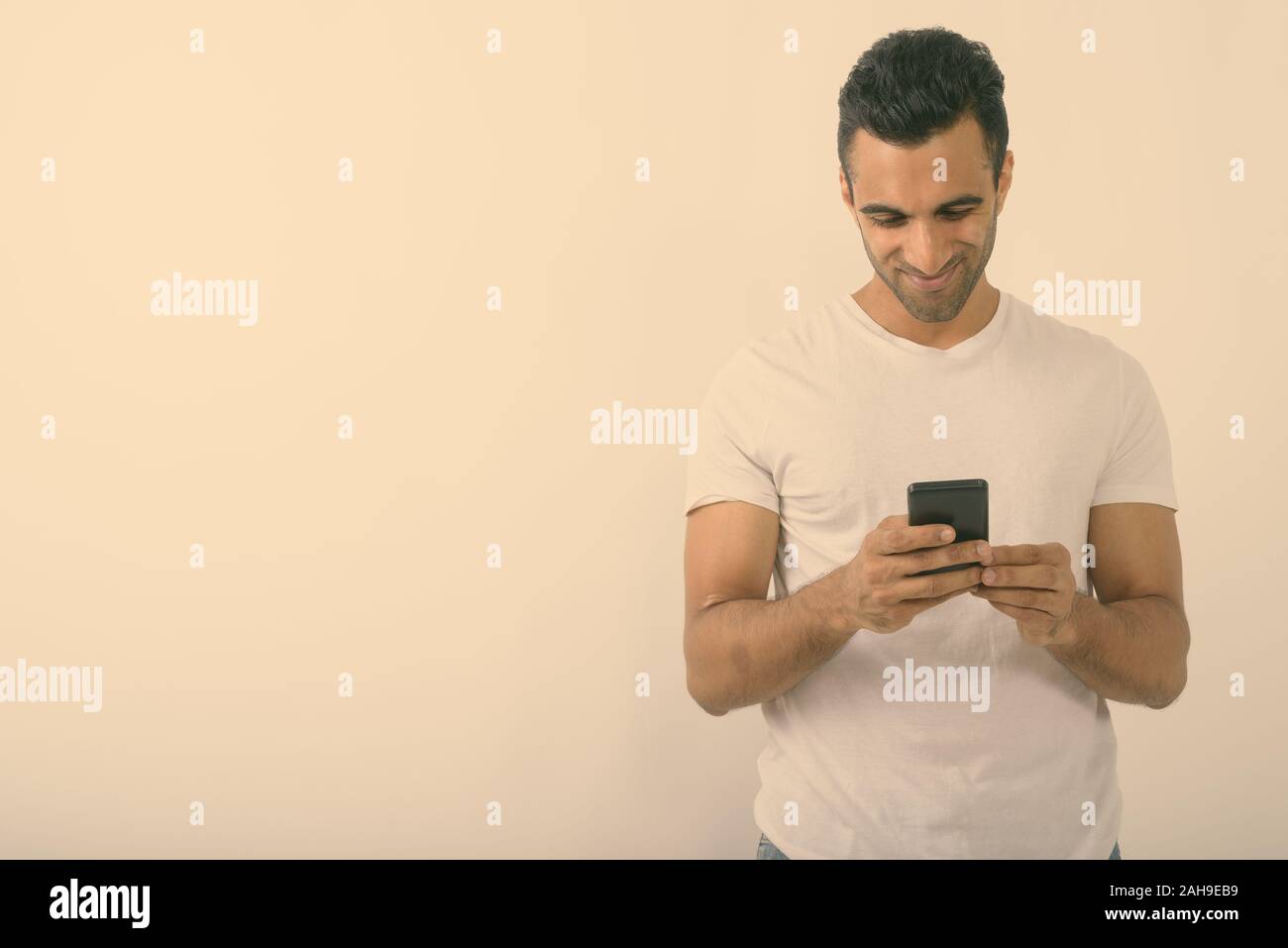 Young handsome Indian man using mobile phone against white background ...