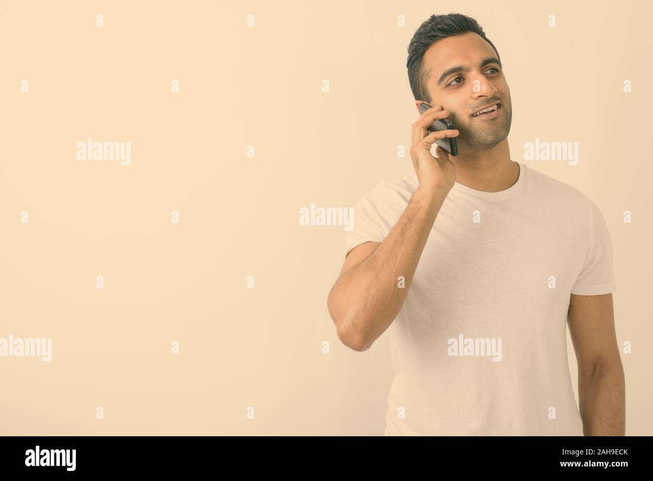 Young handsome Indian man using mobile phone against white background ...