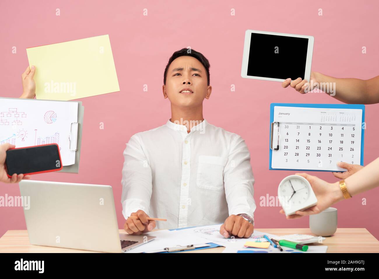 Sad young man sits at desktop, hands with papers, alarm clock, touchpad ...
