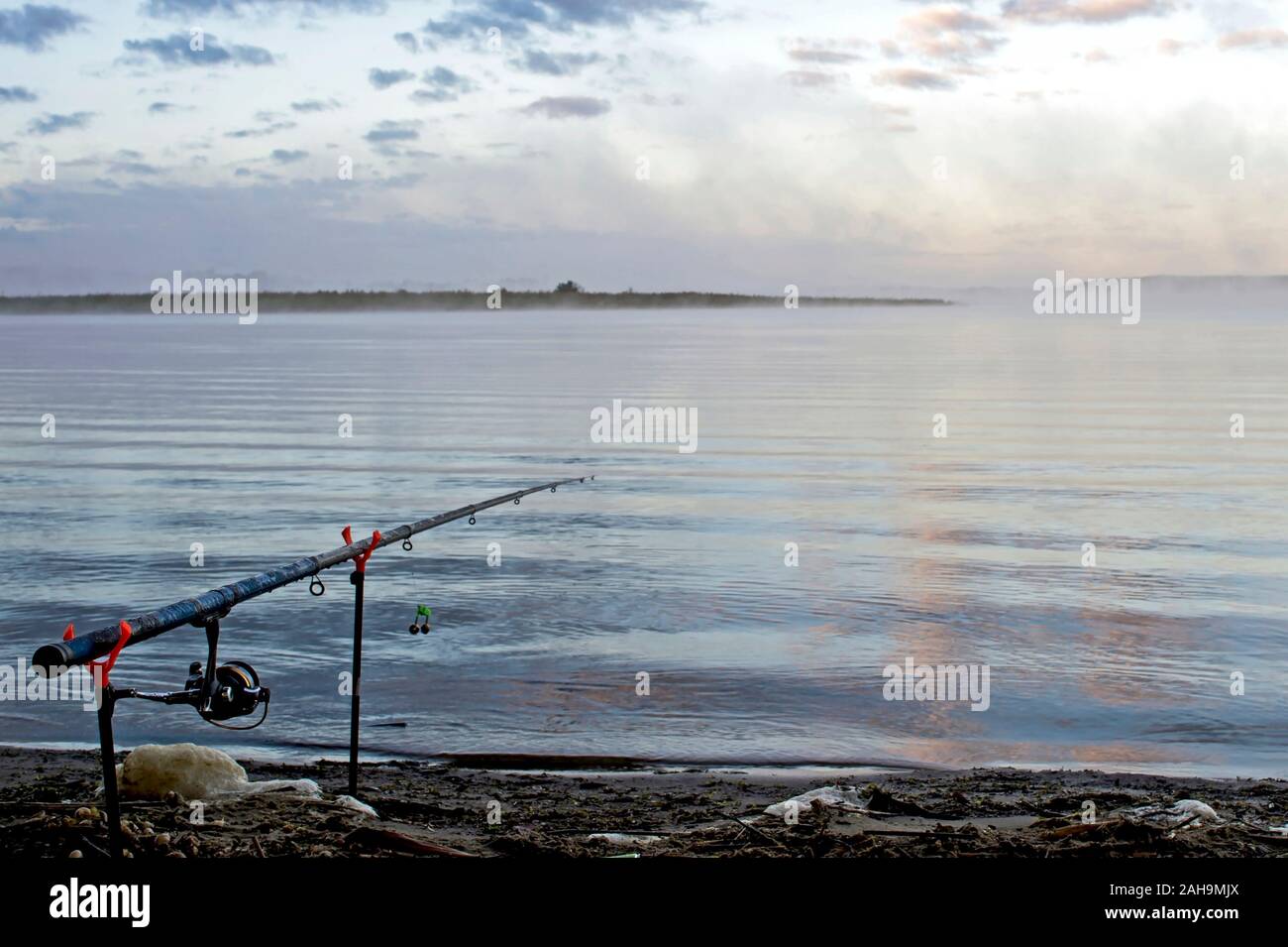 Carp rod with a coil on the background of water with rising thick fog ...