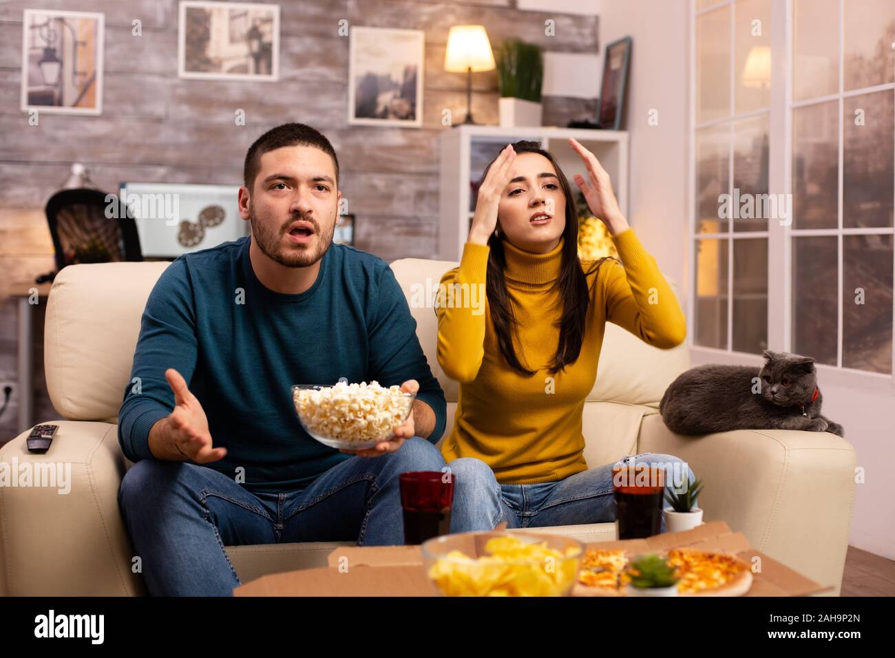 Couple cheering for their favourite team while watching TV and eating ...