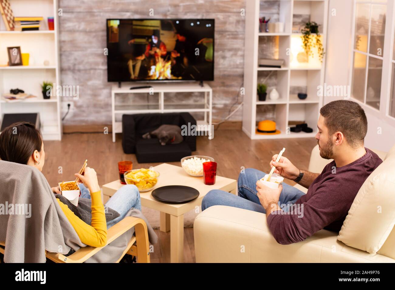 Back view of couple in living room watching a movie on the TV while ...