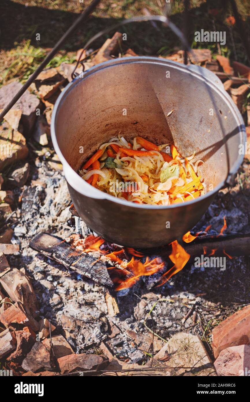 Cooking vegetable stew in large cauldron on camping fire. Sunny day ...