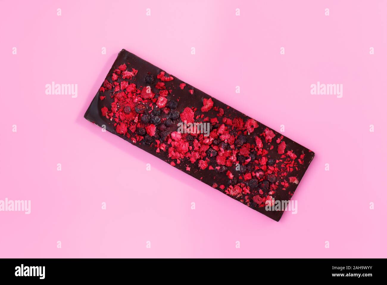 Dark chocolate with dried red berries on bright pink background, top ...