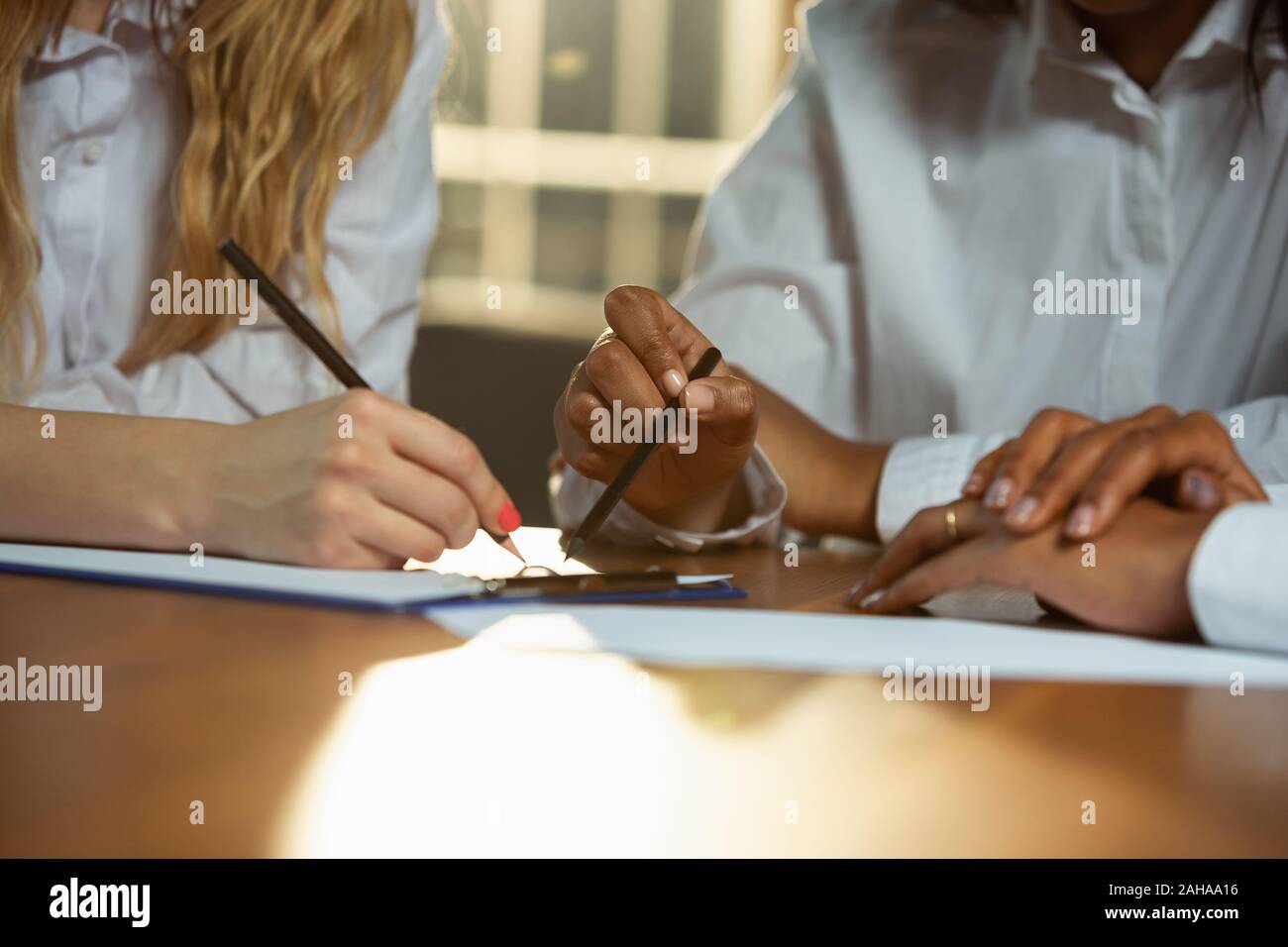 Close up of african-american and caucasian human's hands writing on ...