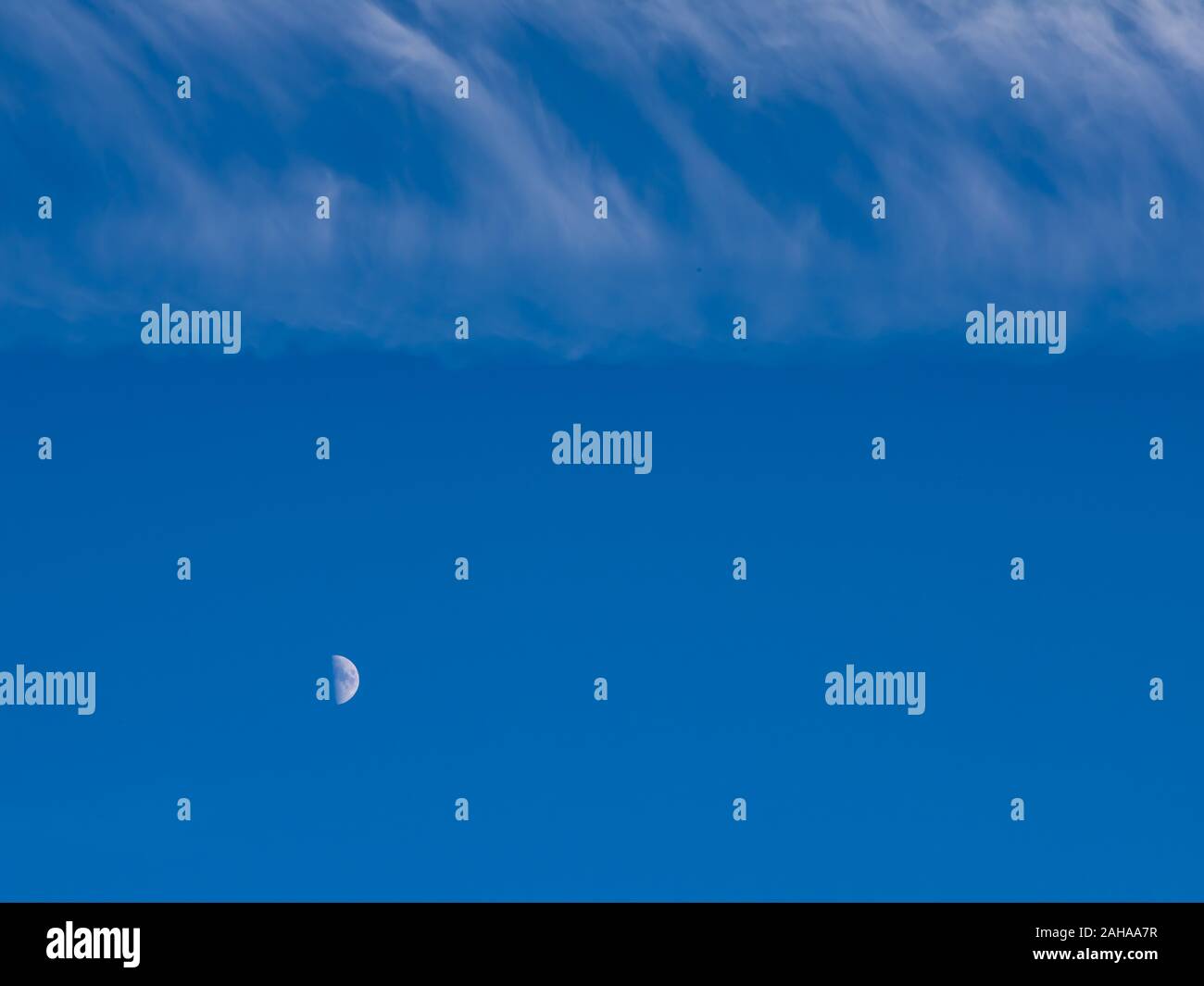 A stripe of clouds in the top half of frame and the half moon in the ...