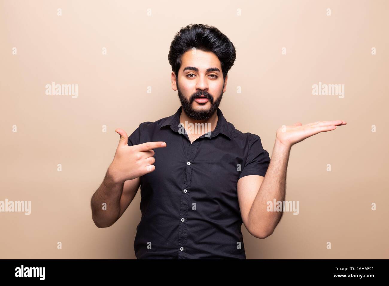 Happy bearded young man pointed on palm on beige background Stock Photo ...