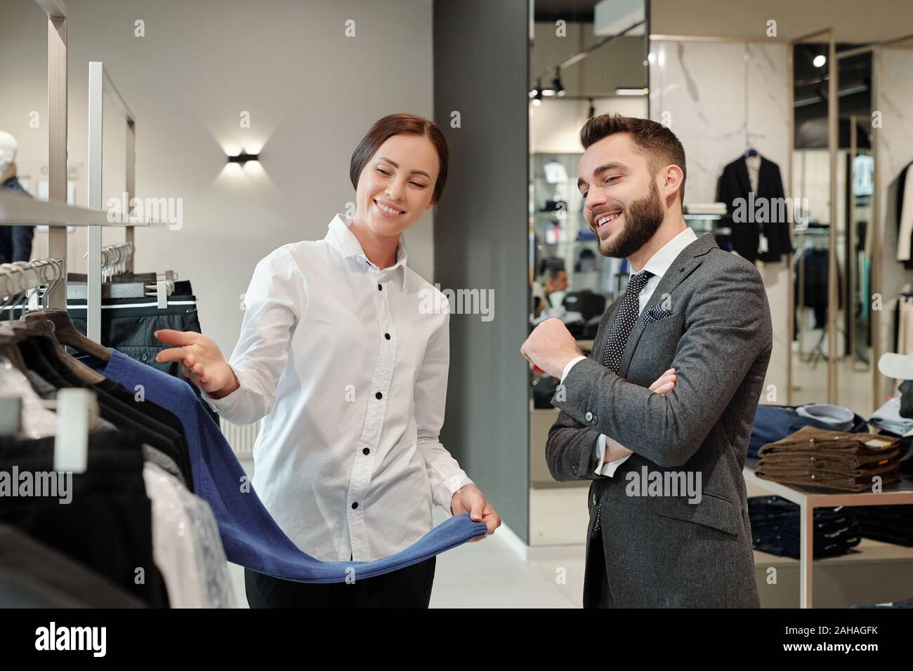 Happy young elegant man in grey suit consulting with shop assistant ...