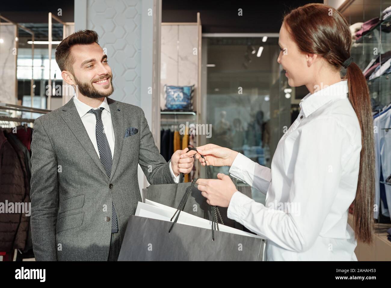 Young shop assistant passing paperbags with new clothes to happy ...