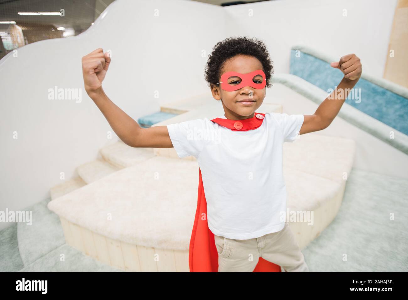 Strong cute little boy of African ethnicity wearing red mantle of super ...