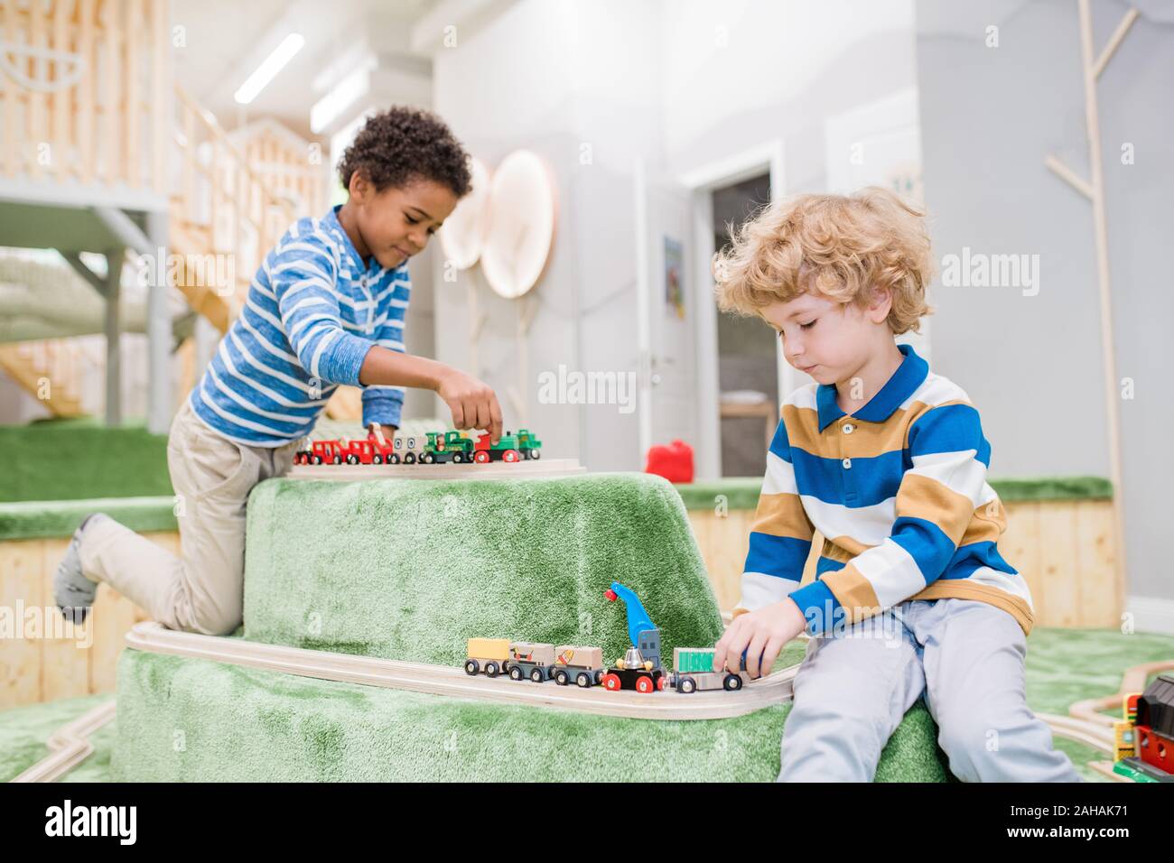 Two intercultural little boys sitting on playground while playing toy ...