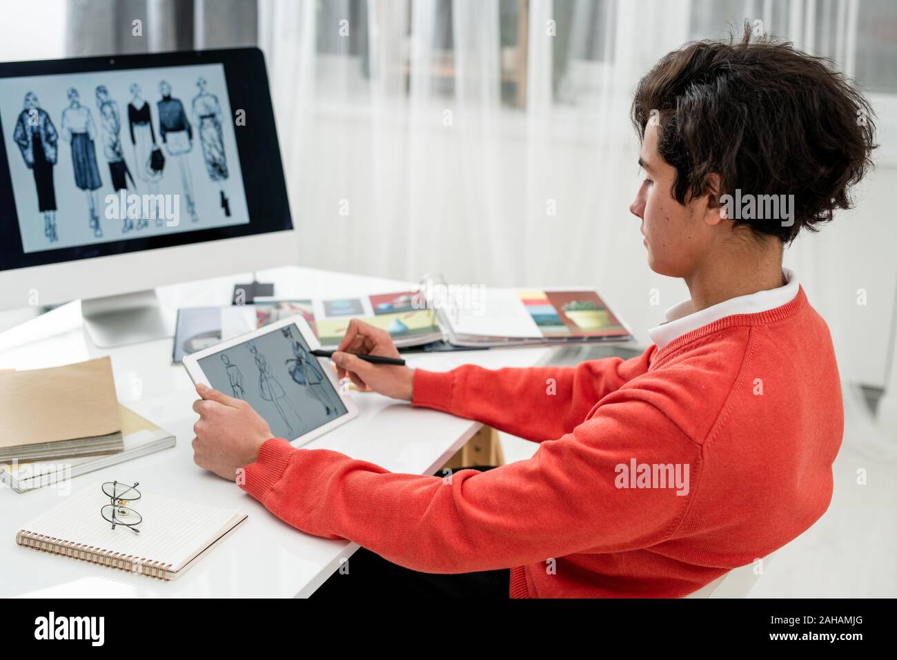 Young fashion designer looking through new models in touchpad by desk ...