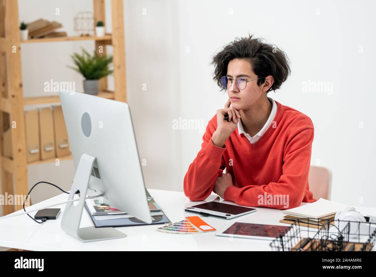 Serious web designer in eyeglasses looking through examples on computer ...
