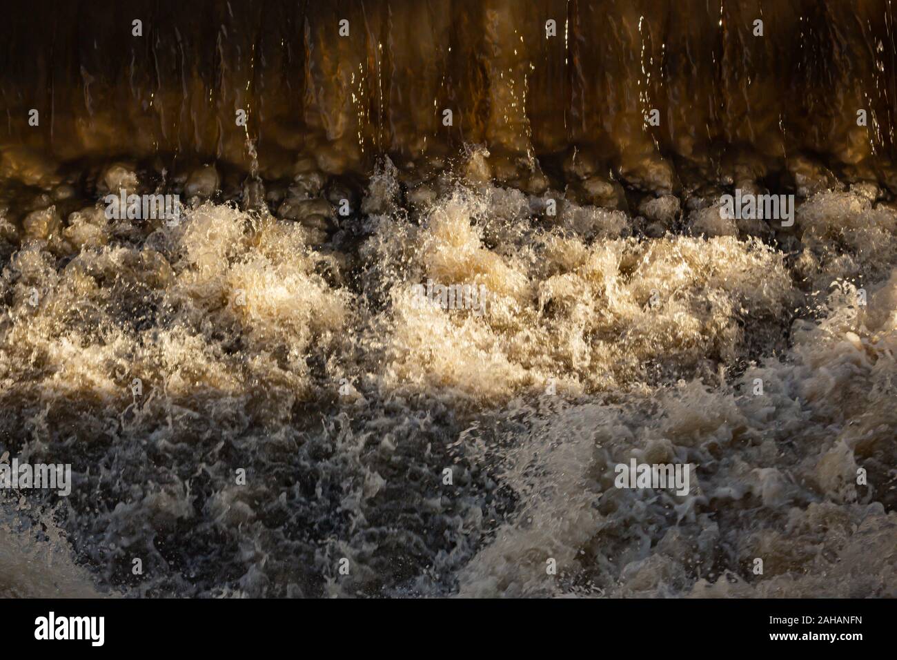 Gusting water under a weir during a flood, sunlight illuminating the ...