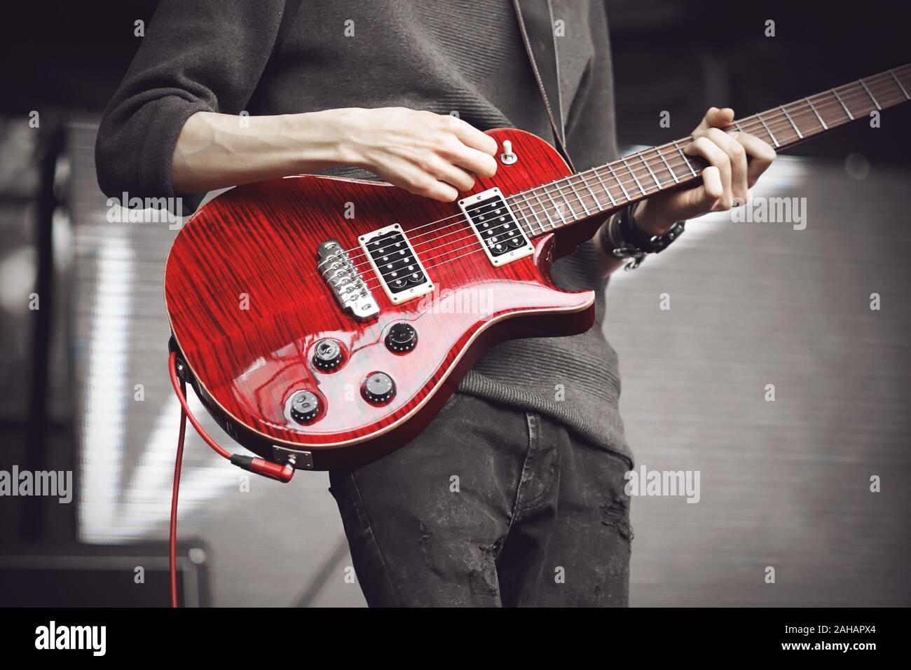 A guitarist in a grey sweater and dark jeans with a bright red electric ...