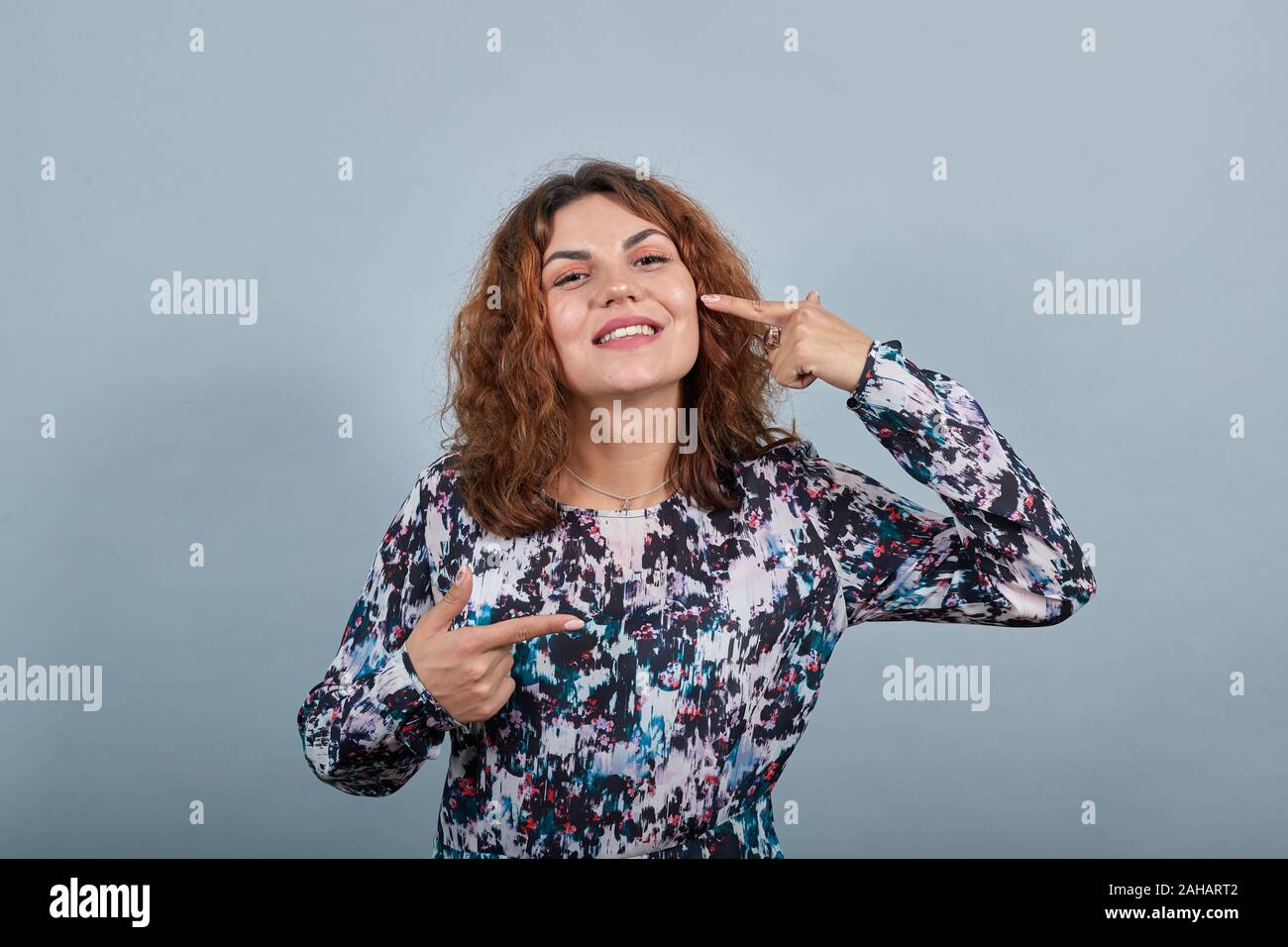 Cheerful caucasian young woman pointing finger at cheeks, looking happe ...