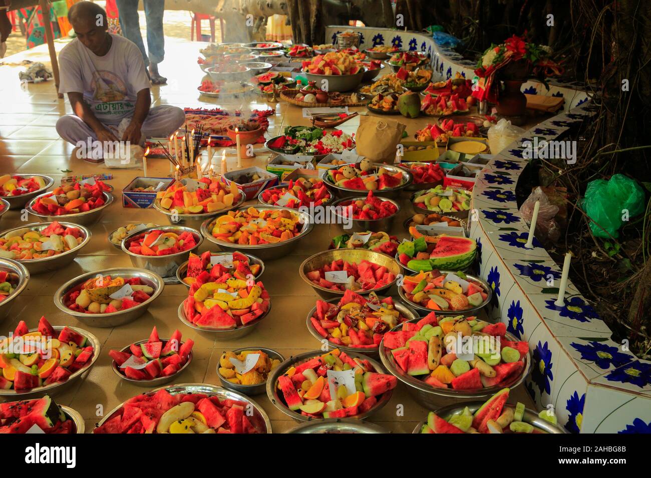 Priest sits beside arrays of offerings placed under the ancient banyan ...
