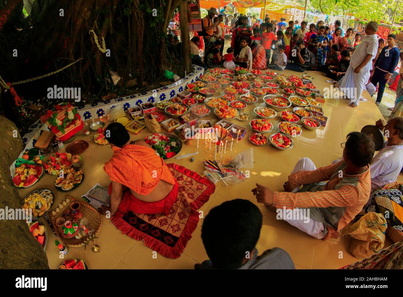 Priest sits beside arrays of offerings placed under the ancient banyan ...