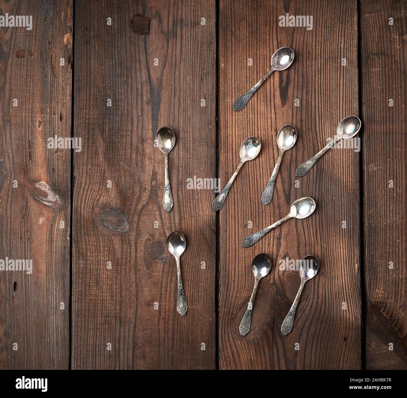 set of small metal teaspoons on a brown wooden table, top view, copy ...