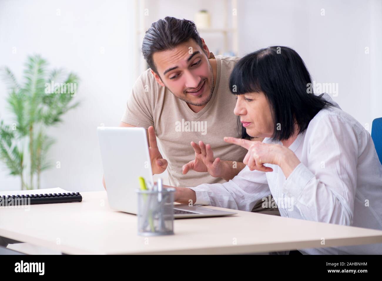 Young male employee explaining to old female colleague how to use ...