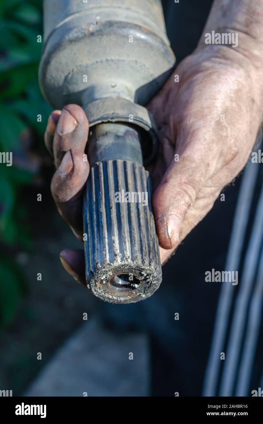 Used driveshaft of a car. A man holds in his hand a rusty drive shaft ...