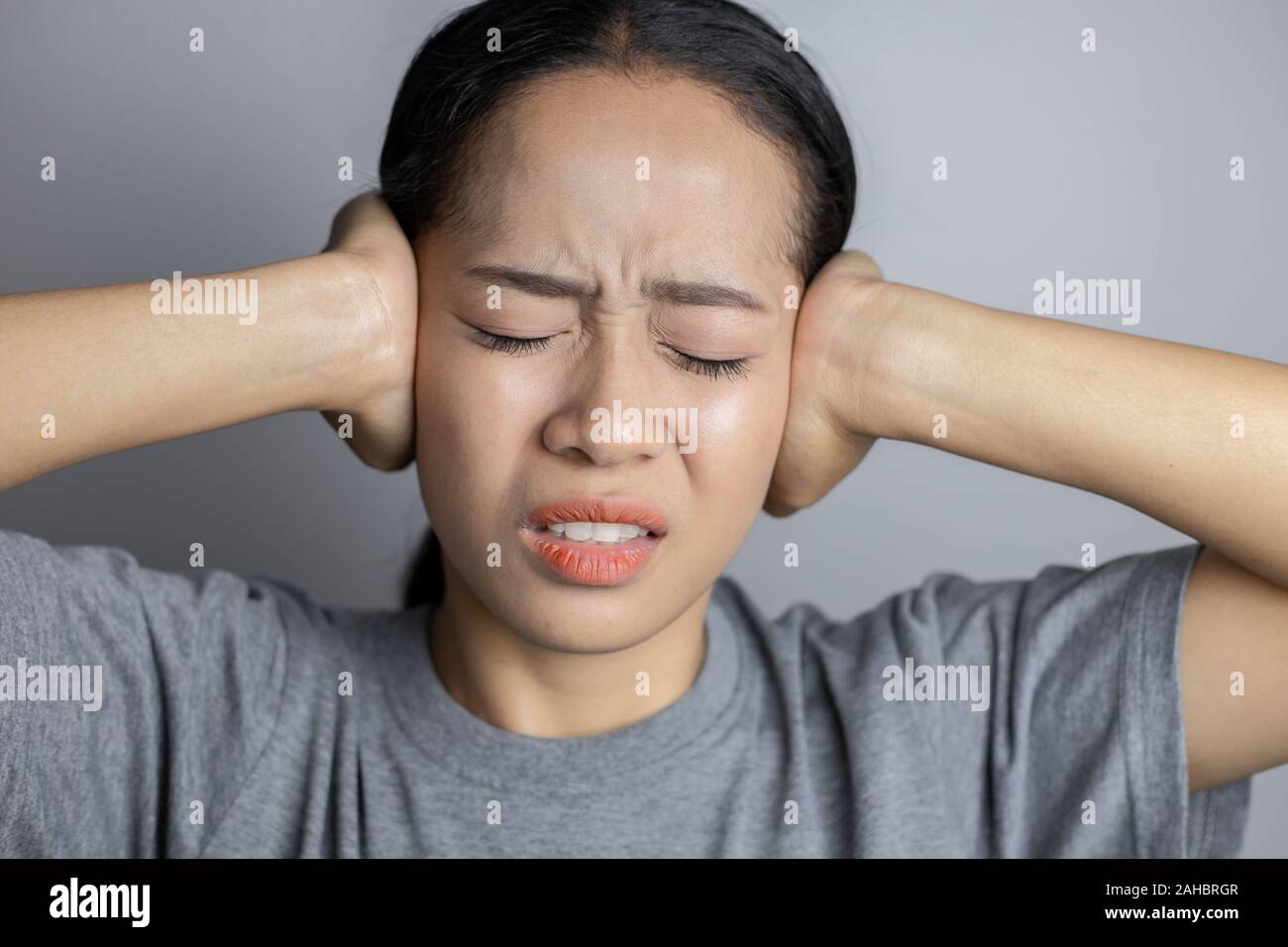 Young woman with of earache on a gray background. Asian woman is ...