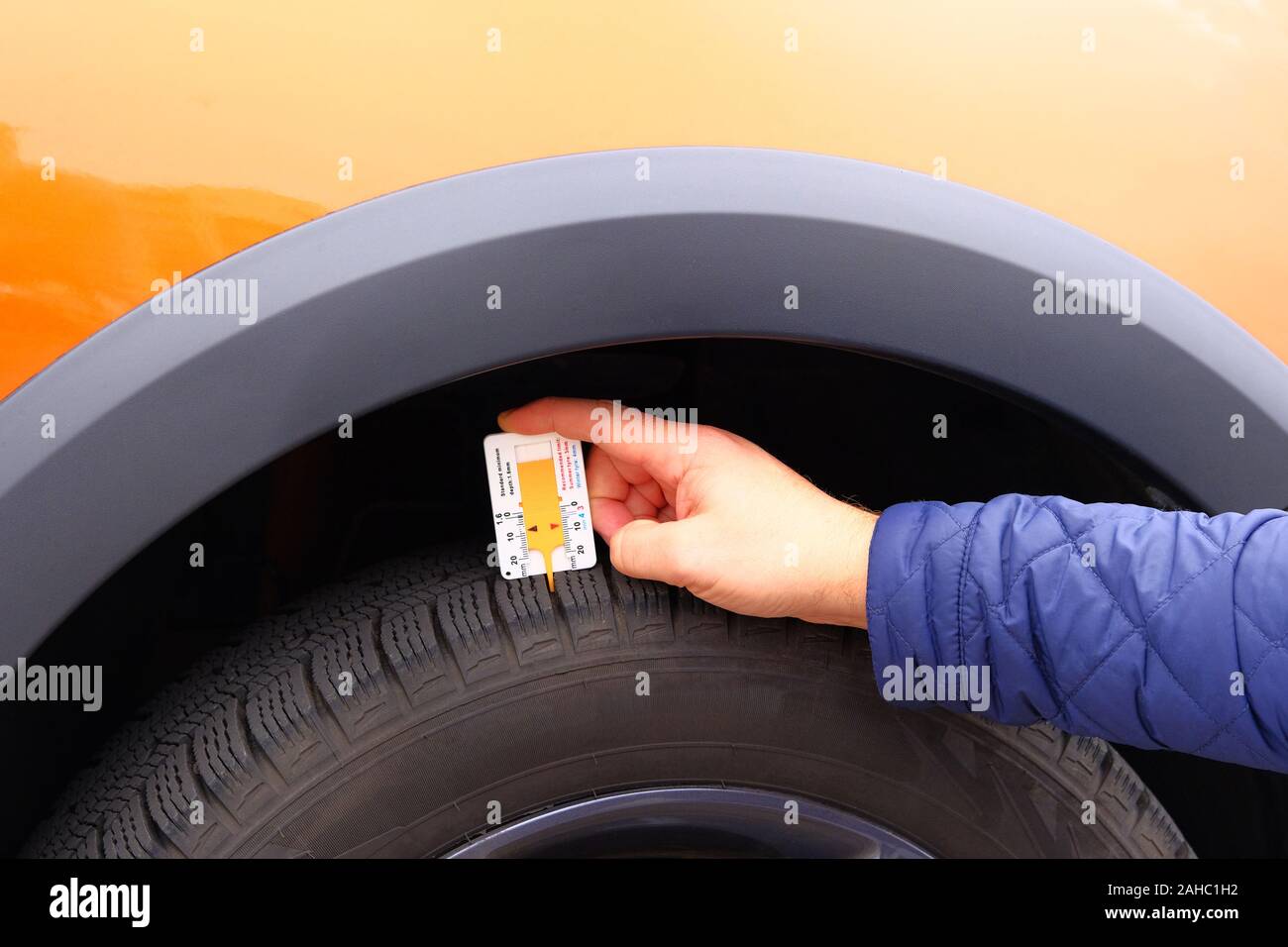 Measuring profile in hand. Tread depth meter at tire in orange car. Man ...