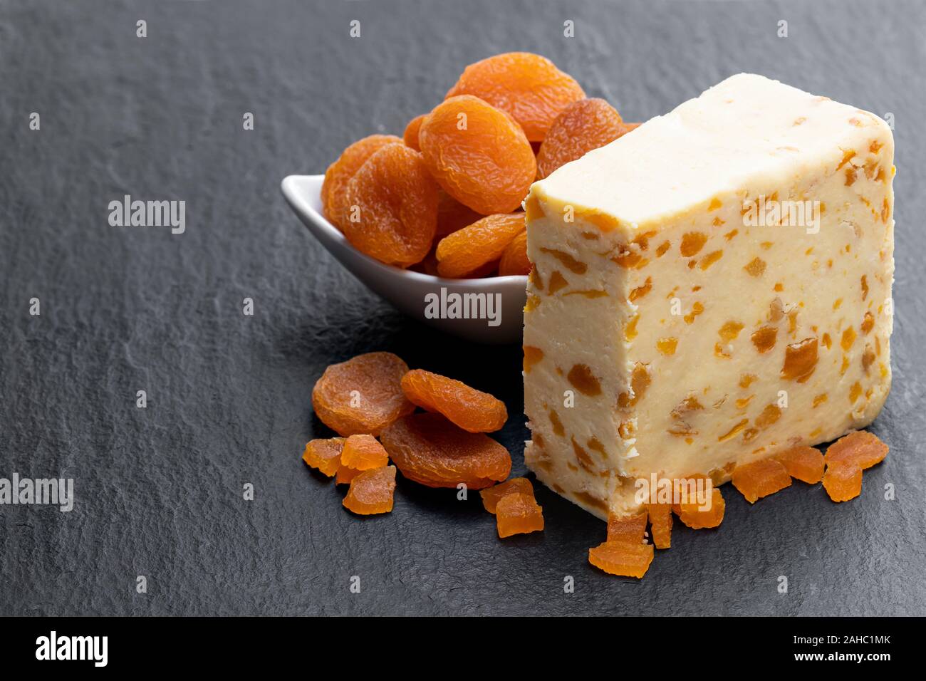 Traditional cheddar cheese with dry apricot on black stone background ...