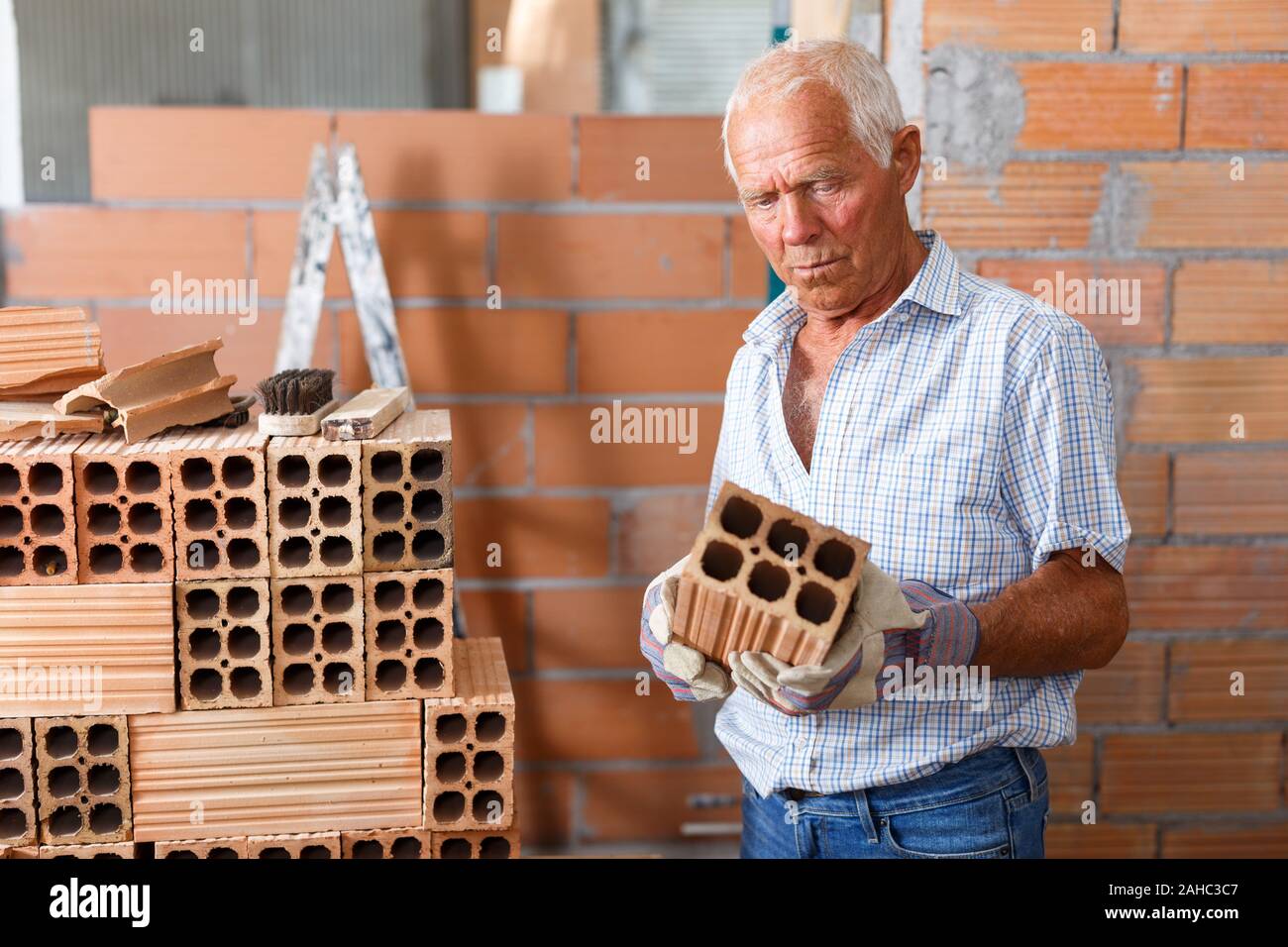 Skillful older man inspecting brick for installing wall in building ...